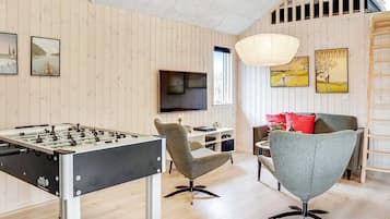 Quarto com mesa de futebol, sofá, televisão e obras de arte nas paredes.