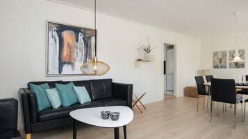 Uma sala de estar moderna com um sofá de couro preto, uma mesa de centro redonda e um espaço de refeições com uma mesa branca e cadeiras pretas.