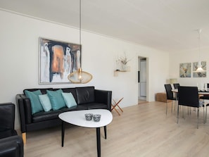 Uma sala de estar moderna com um sofá de couro preto, uma mesa de centro redonda e um espaço de refeições com uma mesa branca e cadeiras pretas.
