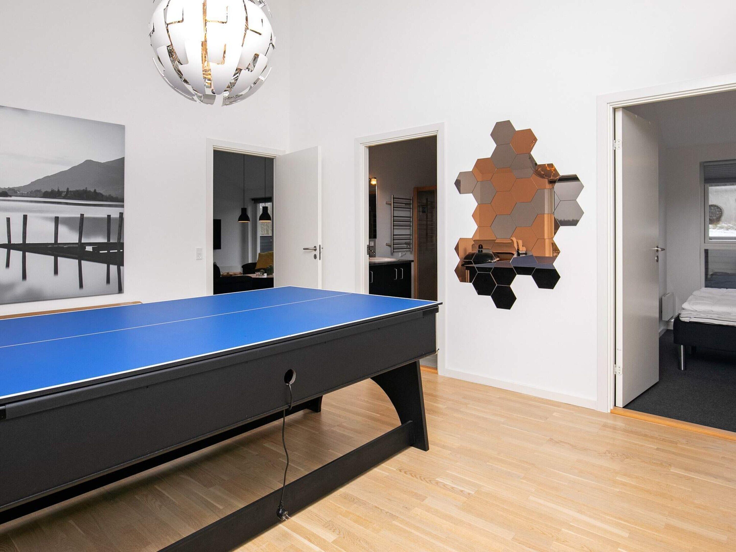Quarto com mesa de pingue-pongue, uma obra de arte na parede e porta que dá para outro cômodo.