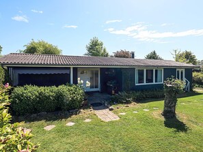 Uma casa térrea com fachada azul escura, telhado de telhas e varanda frontal.
