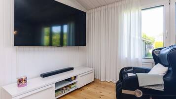 Uma sala de estar moderna com TV de tela plana fixada na parede, um rack branco, um sofá de couro e uma janela grande com cortinas.