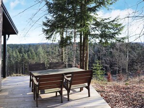 Um deck de madeira com mesa e bancos, com vista para uma área arborizada.