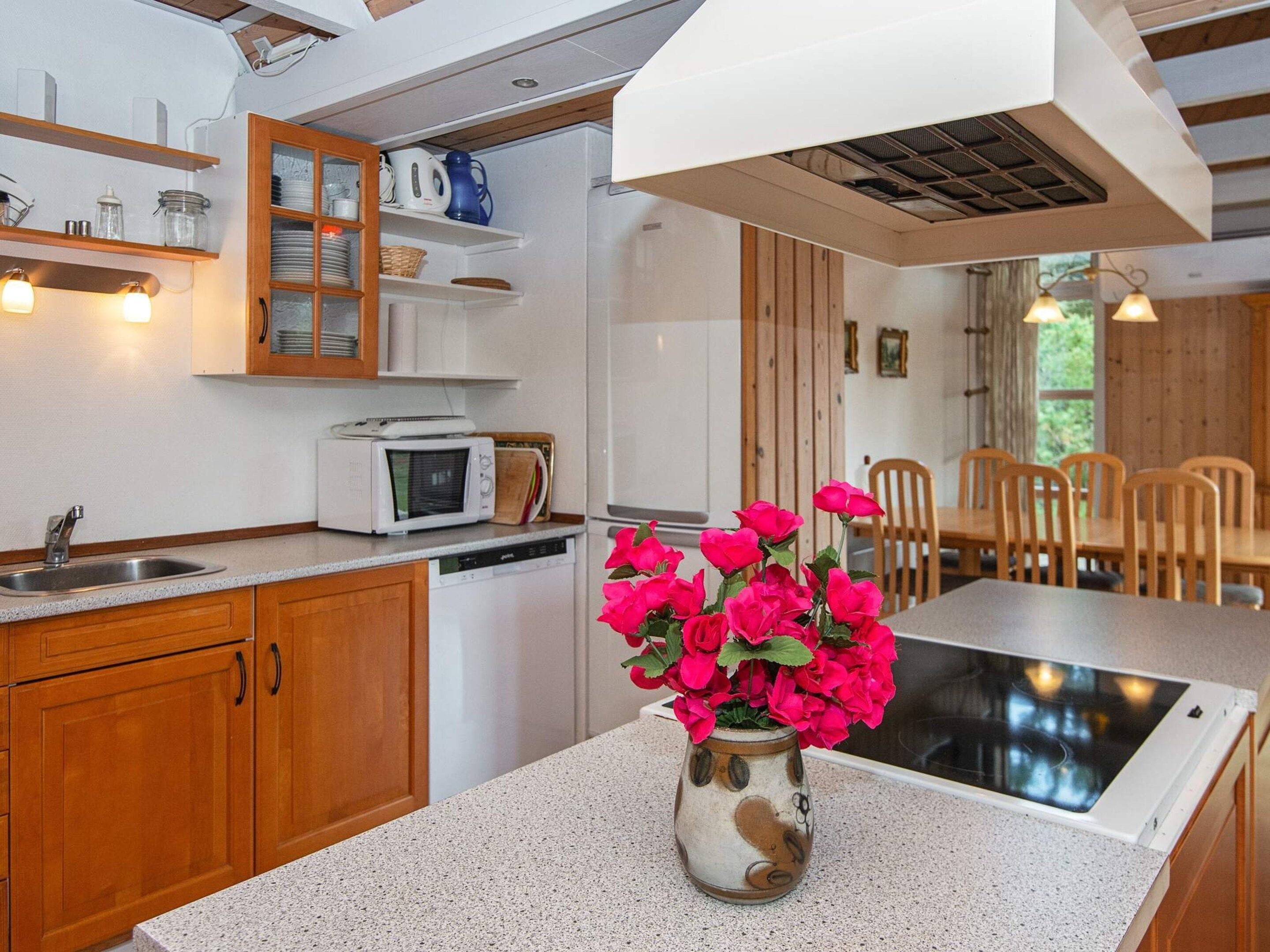 Cozinha com armários de madeira, micro-ondas, lava-louças e um vaso com flores na bancada.