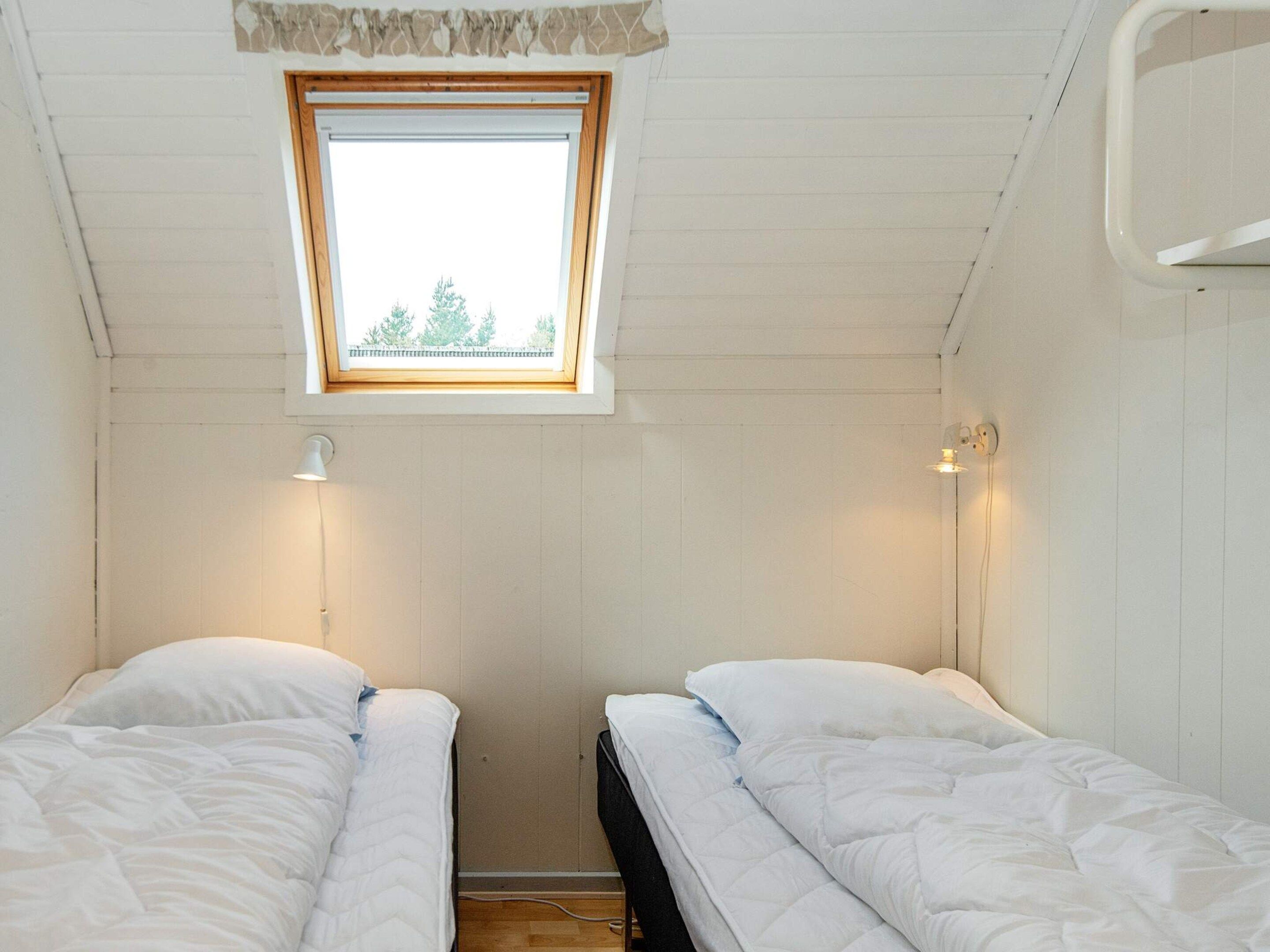 Quarto pequeno com duas camas, um claraboia e um aplique na parede.