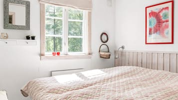 Quarto com uma cama grande, janela com cortinas, mesa de cabeceira, espelho fixado na parede e quadro emoldurado.