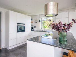 Uma cozinha moderna com armários brancos, bancada de granito, luminária pendente e janela com vista para o verde.
