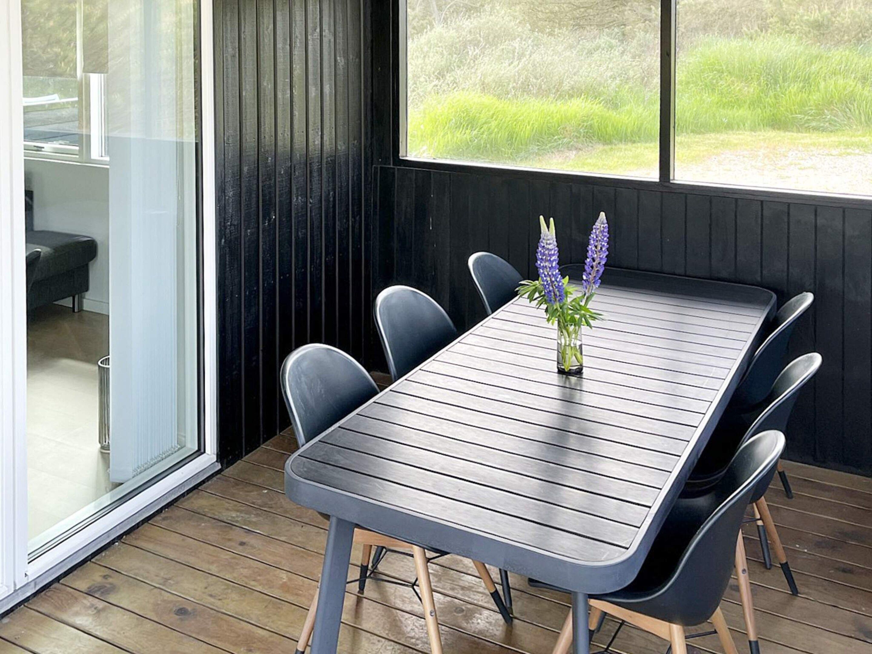 Uma área de refeições moderna com uma mesa de madeira escura, seis cadeiras e um vaso com flores roxas.