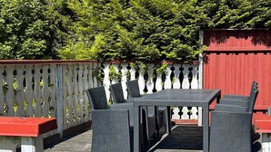 Um pátio externo com uma mesa e cadeiras, cercado por uma cerca branca de piquete e uma parede vermelha.