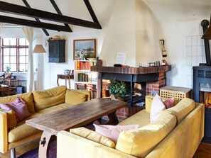 Uma sala de estar aconchegante com lareira, sofás amarelos, uma mesa de madeira e uma estante de livros.