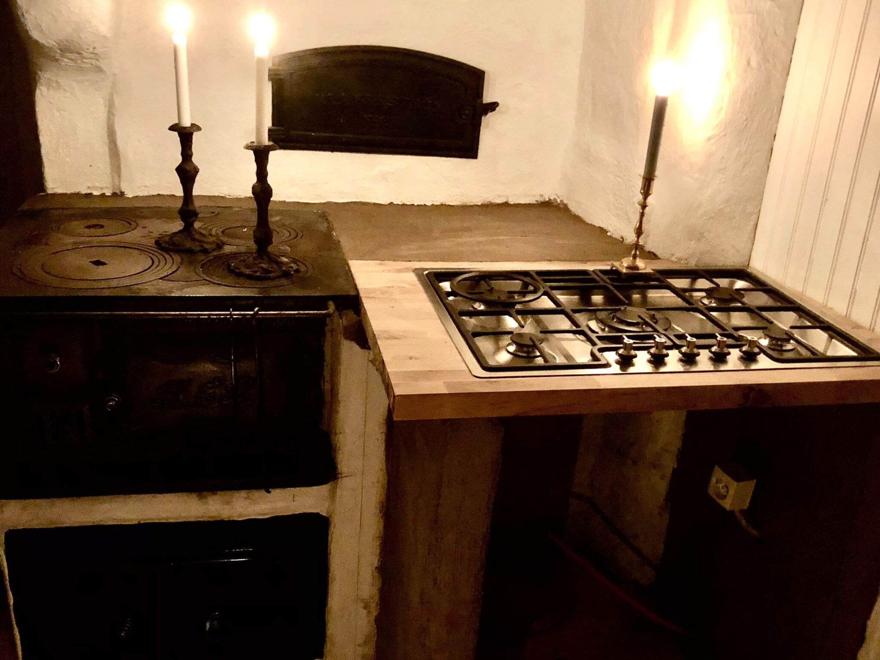 Cozinha com fogão e cooktop a gás, duas velas acesas e uma janela com moldura preta.