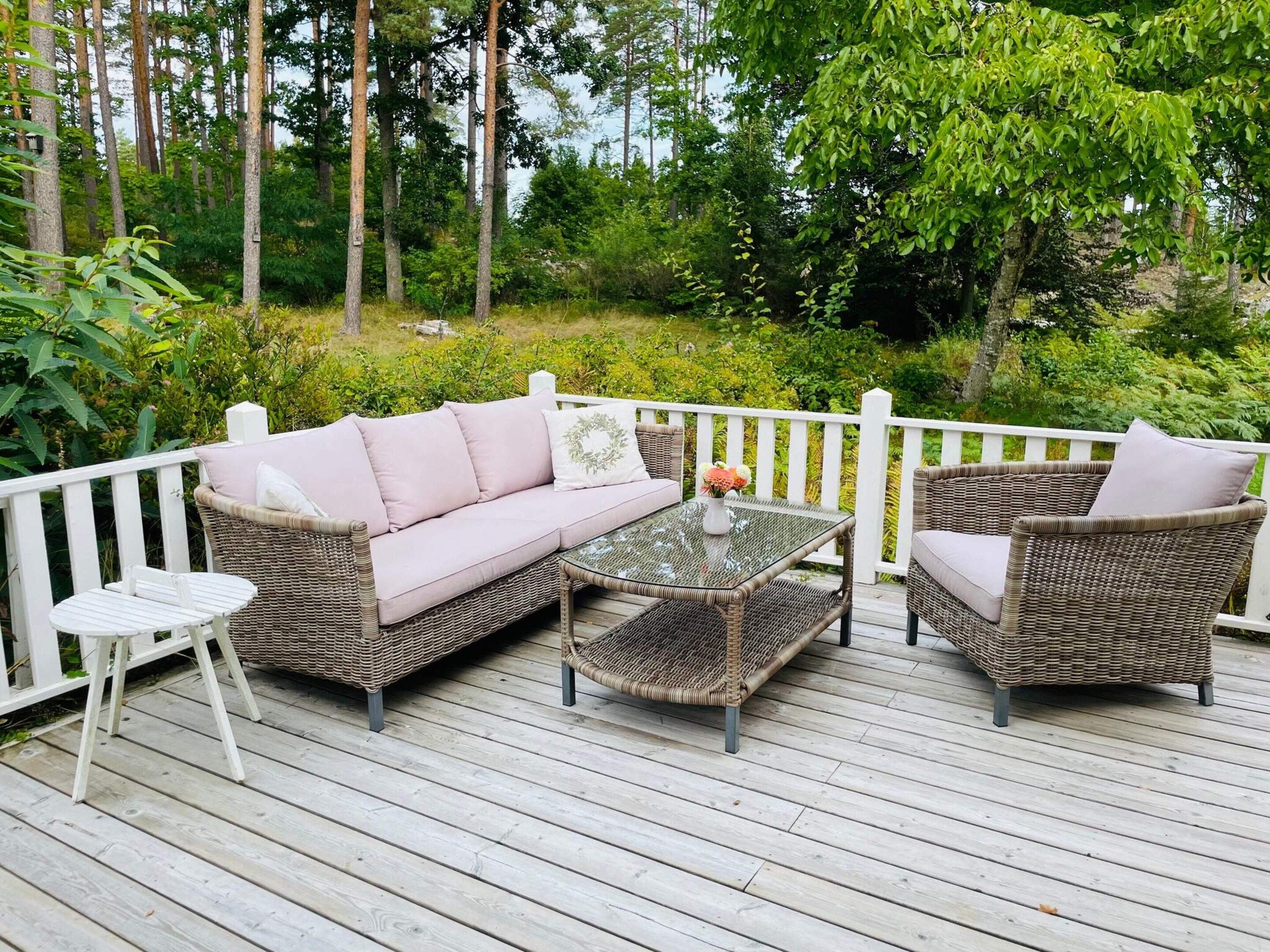 Um deck ao ar livre com mobiliário de vime, incluindo um sofá e cadeiras, e uma mesinha com um vaso de flores.