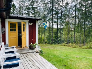 Uma cabana com deck de madeira, porta amarela e uma bandeira azul.