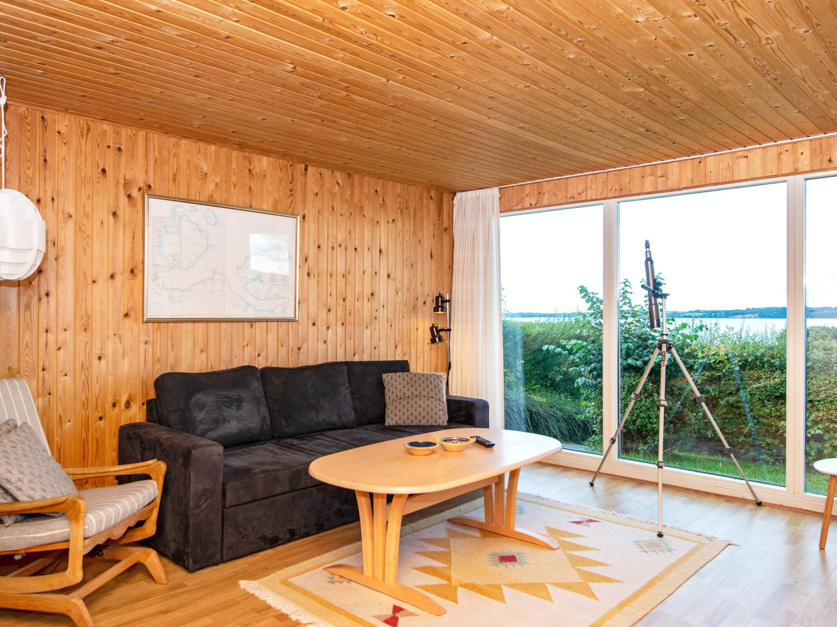 Quarto com teto de madeira, uma grande janela com um tripé, sofá preto, mesa de centro de madeira e um mapa na parede.