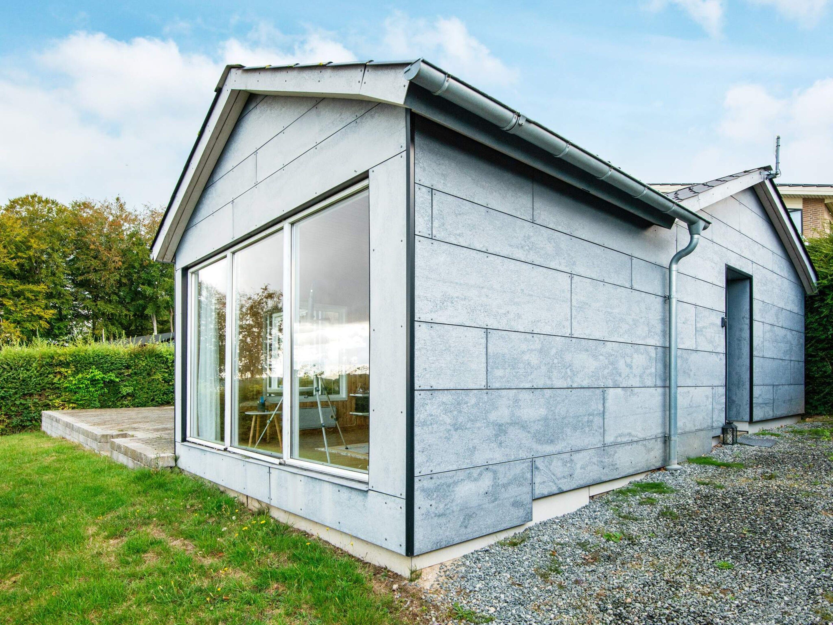 Uma casa moderna com uma grande janela de vidro, telhado inclinado e entrada com calçamento de brita.