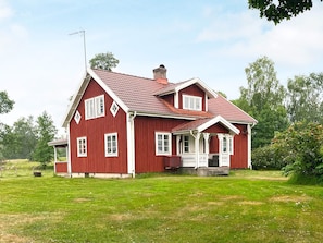 Uma casa vermelha de dois andares com varanda, chaminé e um gramado grande.