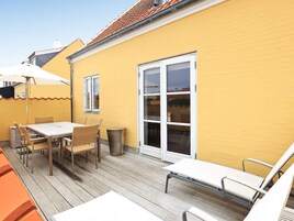 Um edifício amarelo com uma janela grande, uma mesa e cadeiras, e uma área externa coberta.