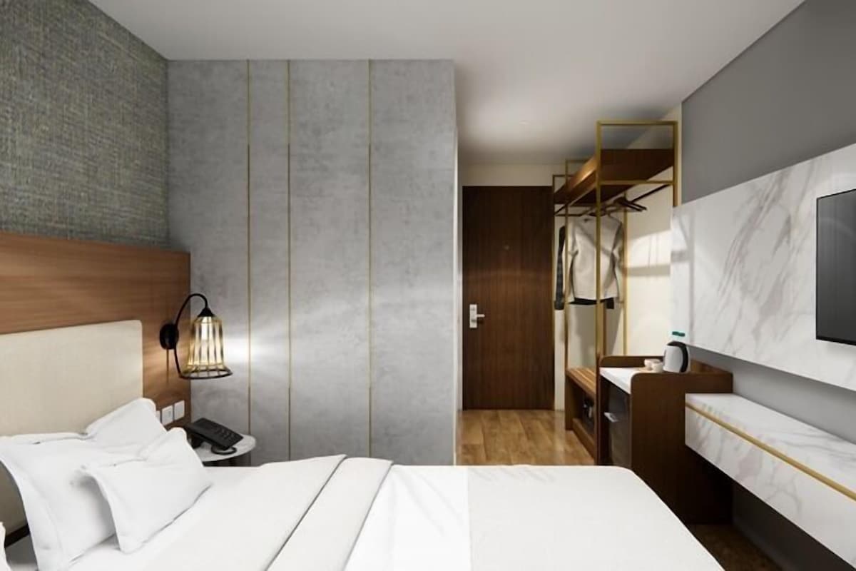 Quarto de hotel moderno com cama, mesa de cabeceira, abajur, guarda-roupa e televisão fixada na parede.