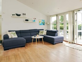 Uma sala de estar moderna com um sofá seccional azul escuro, uma mesinha de centro redonda e uma janela grande com vista para o verde.