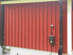 Parede de metal corrugado vermelho com uma caixa elétrica preta e um cabo descendo por ela.