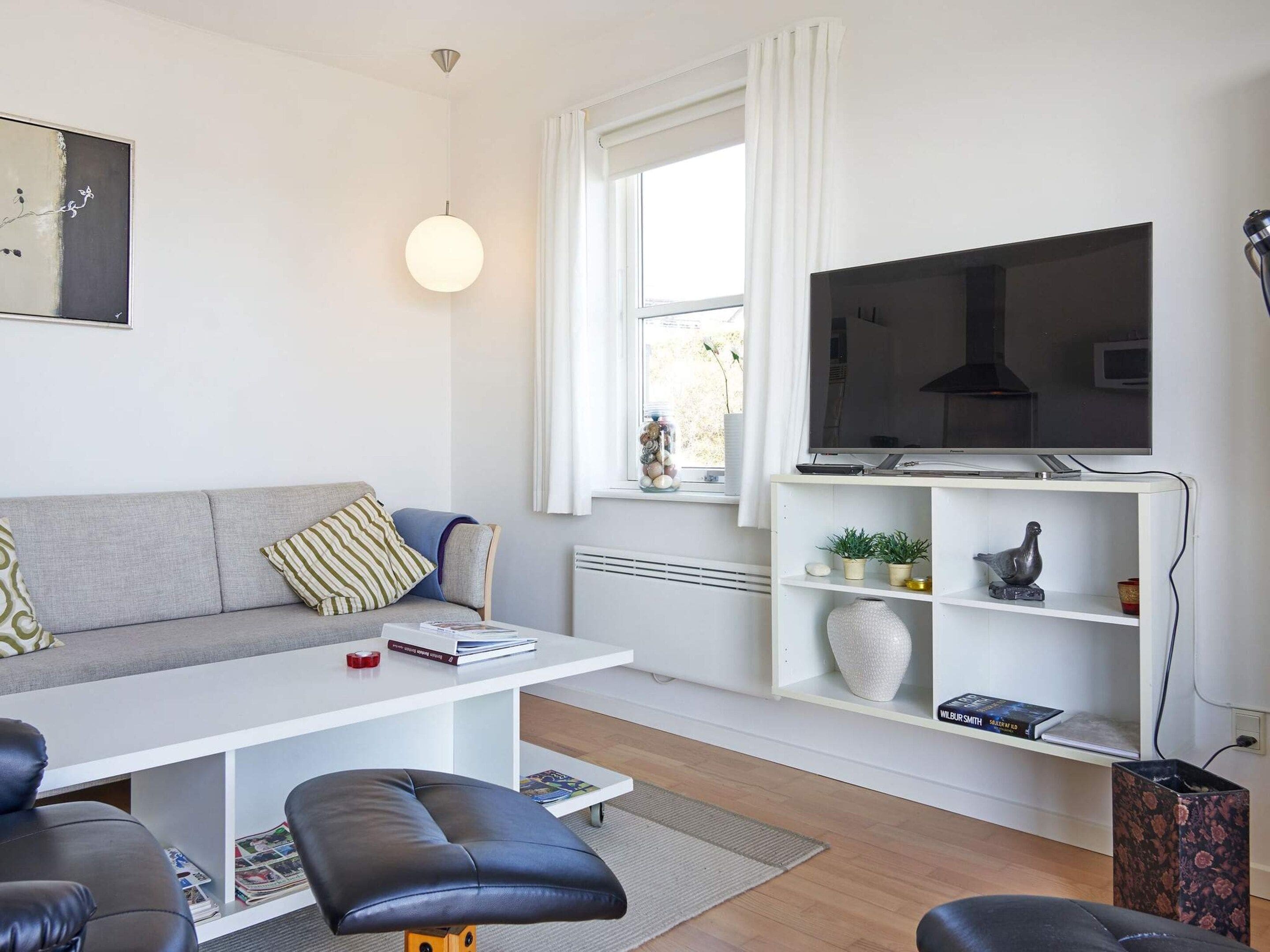 Uma sala de estar moderna com um sofá, uma mesa de centro, uma televisão e uma estante de livros.