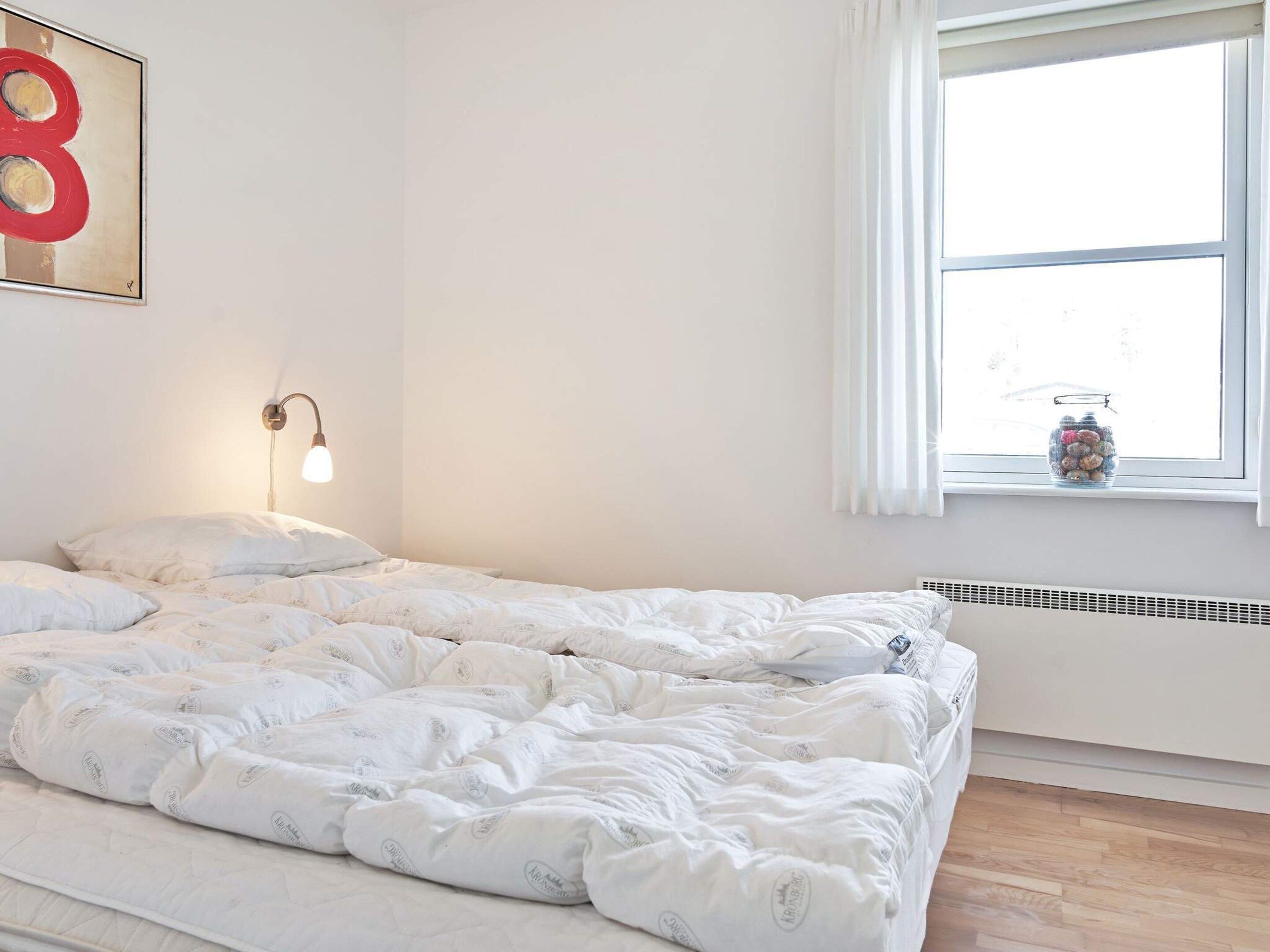 Quarto com cama, luminária na parede, janela com cortinas e radiador.