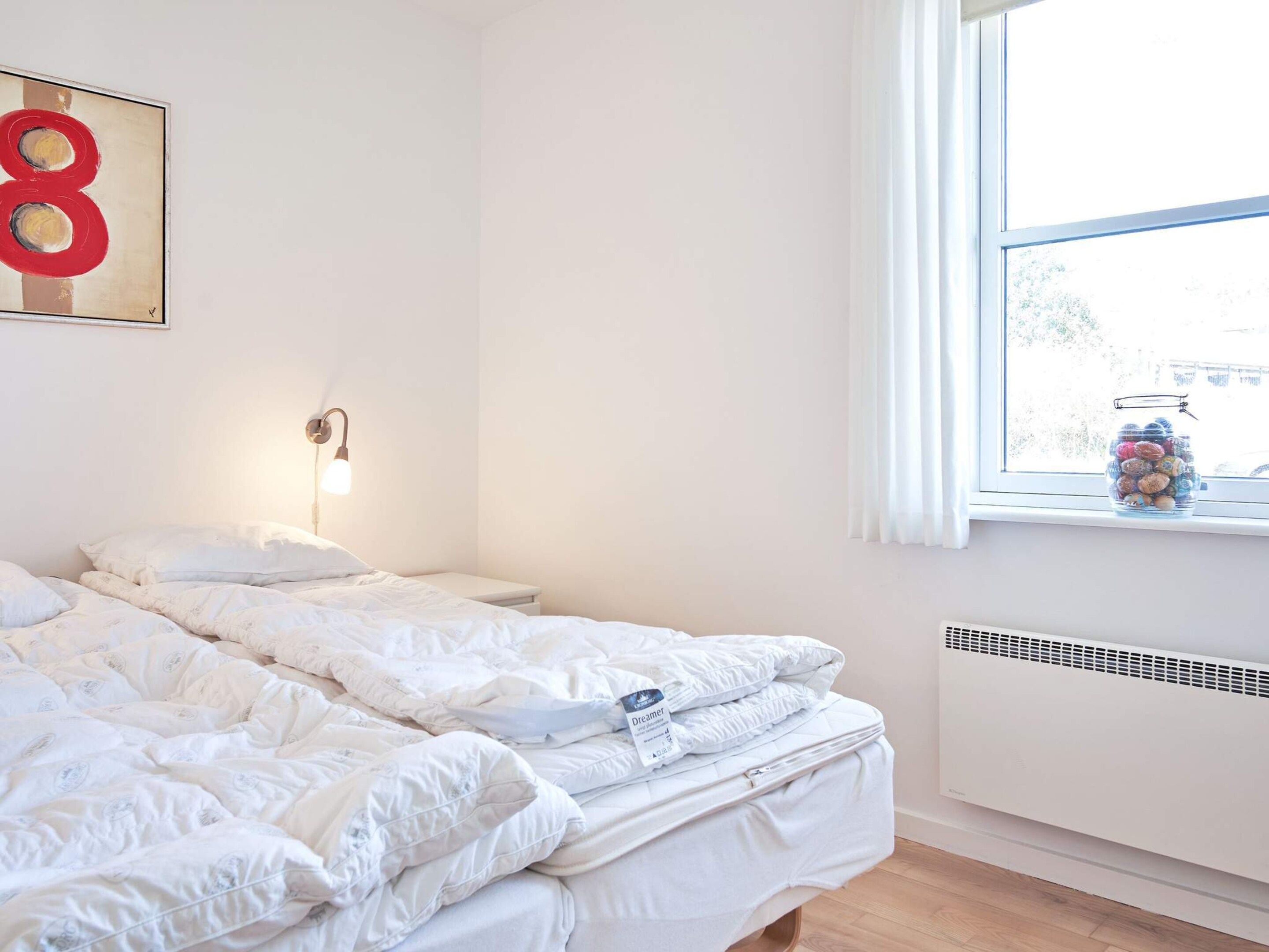 Quarto com cama, mesa de cabeceira, relógio de parede, janela com vista e radiador.