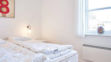 Quarto com cama, mesa de cabeceira, relógio de parede, janela com vista e radiador.