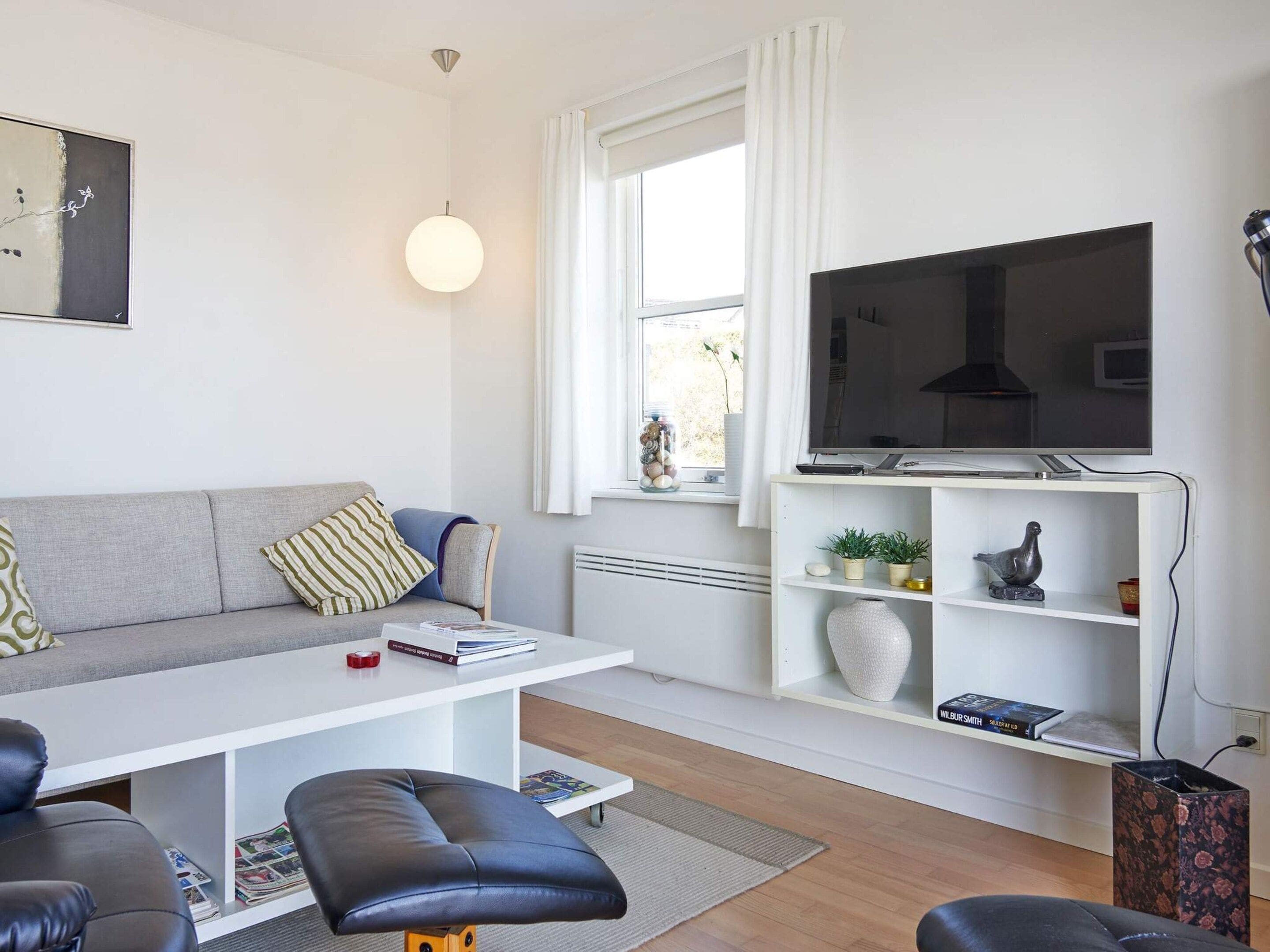 Uma sala de estar moderna com sofá, mesa de centro, televisão e estante.
