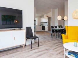 Uma sala de estar moderna com televisão de tela plana, mesa de jantar com cadeiras e uma poltrona amarelo-viva.