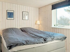 Quarto com cama, paredes de madeira, janela com vista e duas obras de arte emolduradas na parede.