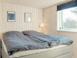 Quarto com cama, paredes de madeira, janela com vista e duas obras de arte emolduradas na parede.