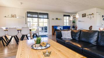 Uma sala de estar aconchegante com uma mesa de centro de madeira, um sofá de couro preto e um espaço de refeições com cadeiras e uma mesa.