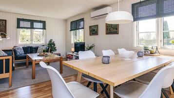 Uma sala de jantar com mesa de madeira, cadeiras brancas e luminária pendente.