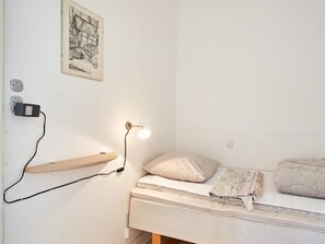 Quarto pequeno com uma cama de solteiro, mesa de cabeceira, luminária na parede e tomada.