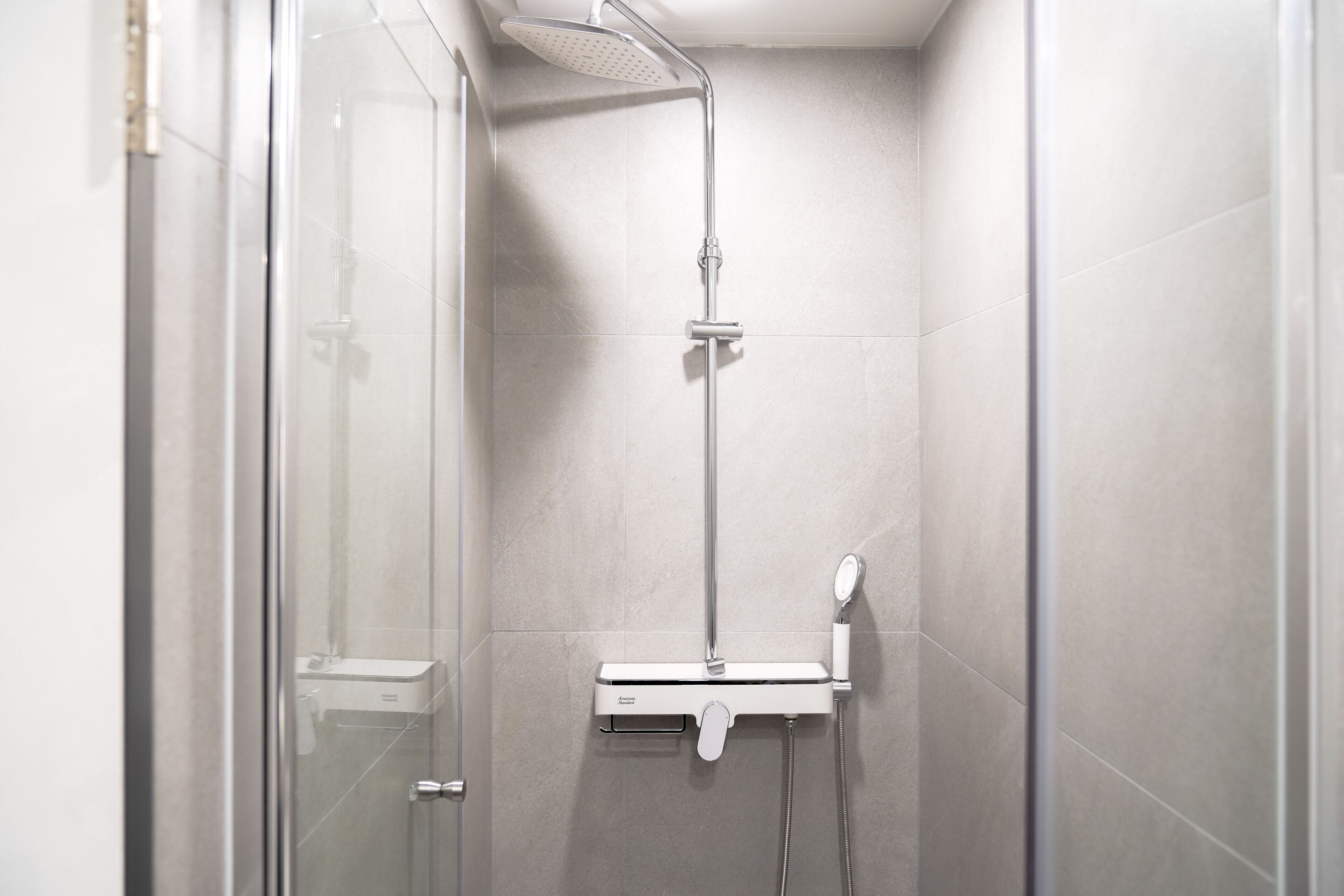 Uma área de chuveiro moderna, com porta de vidro, chuveiro manual e painel de controle na parede.