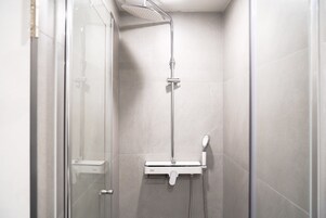 Uma área de chuveiro moderna, com porta de vidro, chuveiro manual e painel de controle na parede.