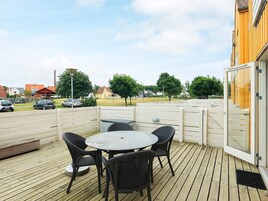 Um pátio externo com mesa redonda e quatro cadeiras, cercado por um deck de madeira e uma cerca branca.