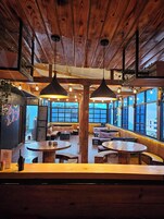 Interior rústico com vigas de madeira, luminárias pendentes e janelas amplas com vista.