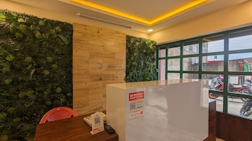Um balcão de recepção com um código QR para pagamento, envolto em um painel de madeira e uma parede coberta de folhagem verde.