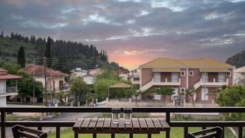 Uma varanda com uma mesa e duas cadeiras, com vista para uma área residencial com casas e uma colina ao fundo.