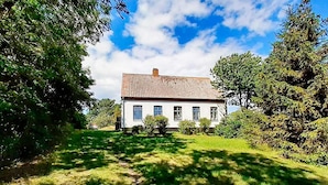 Uma casa de dois andares com telhado de cerâmica, cercada por vegetação exuberante e árvores.