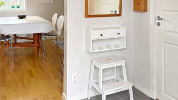 Quarto com mesa branca, cadeiras, um banco branco, uma pequena estante branca e uma porta.