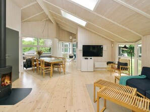 Uma sala de estar ampla com lareira, móveis de madeira, televisão e grandes janelas.