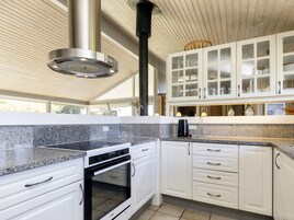 Cozinha moderna com armários brancos, bancadas de granito e coifa de aço inoxidável.
