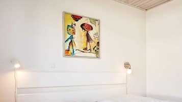 Quarto com cama, mesa de cabeceira, pintura pendurada na parede e duas luzes na parede.