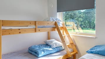 Uma cama beliche com escada de madeira, janela com vista para vegetação e uma cama com lençol listrado.