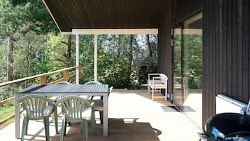 Um deck ao ar livre com mesa e cadeiras, churrasqueira e vista para a floresta.