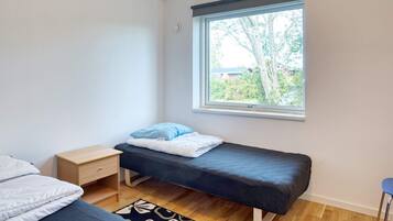 Quarto pequeno com uma cama de solteiro, janela, mesa de cabeceira e uma cadeira.