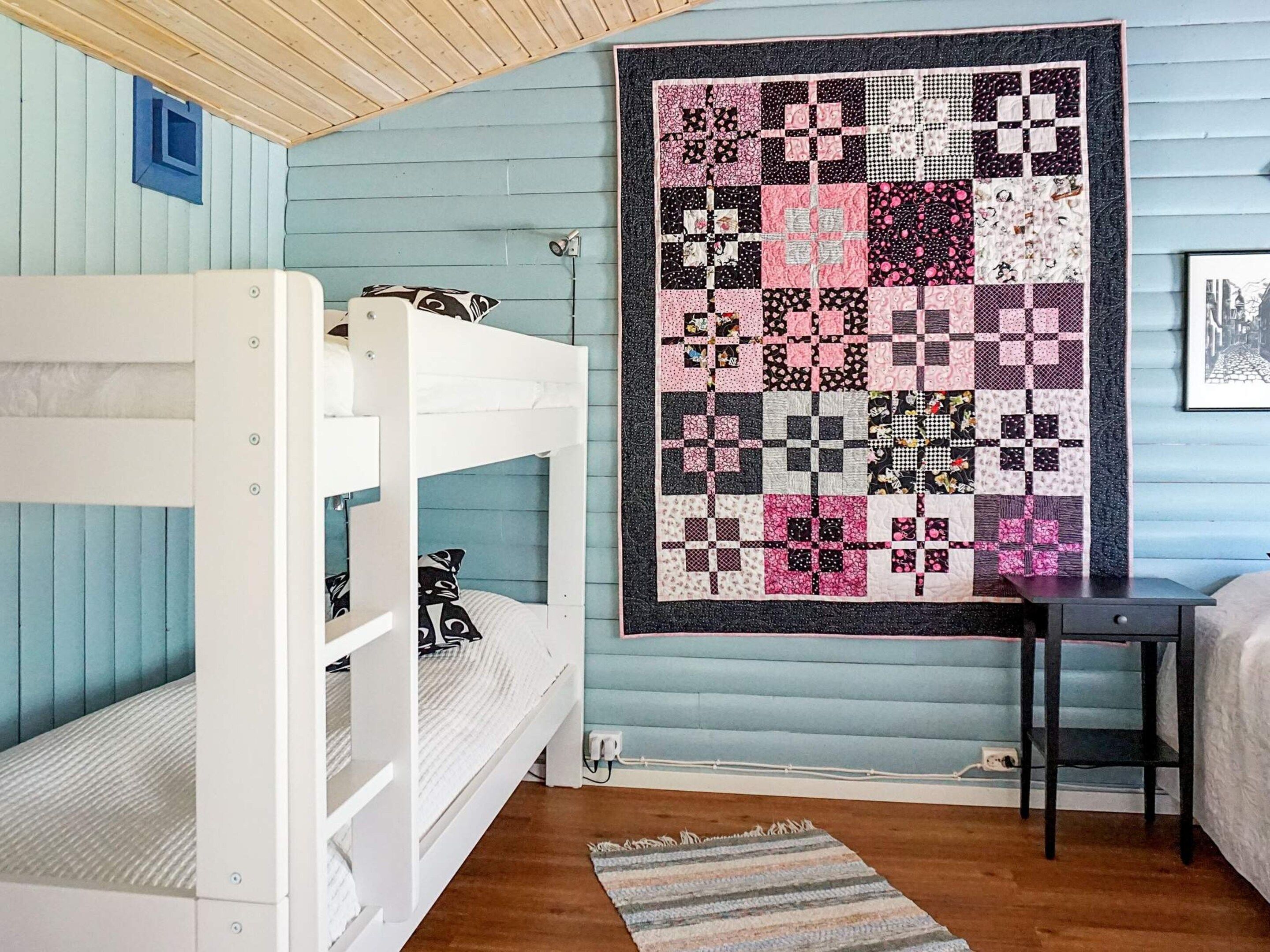 Quarto com beliche, colcha, escrivaninha e cadeira.
